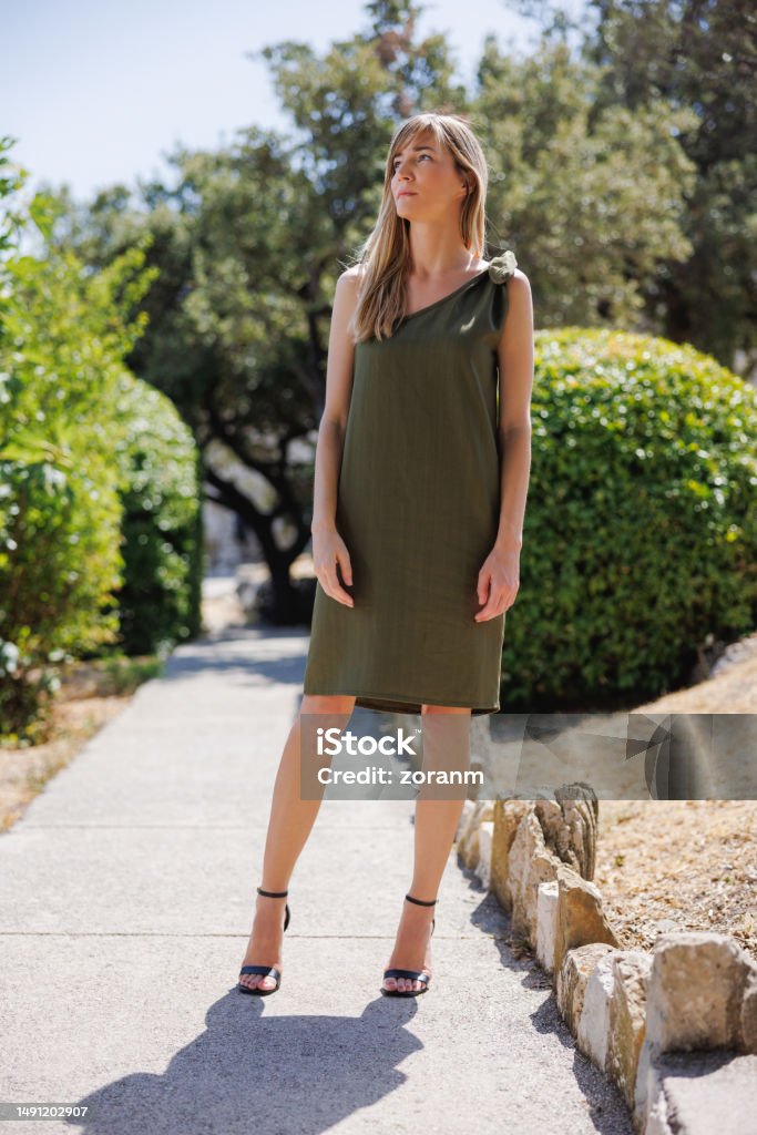 Beautiful Blonde Woman Wearing Olive Sleeveless Mini Dress Standing In