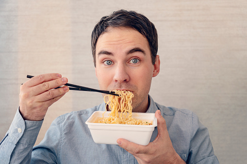 Pria Muda Tampan Ceria Sedang Makan Mie Instan Lezat Dengan Sumpit Foto Stok Unduh Gambar