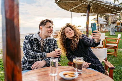 Young Couple Taking Selfies While Drinking Coffee In A Beach Bar In