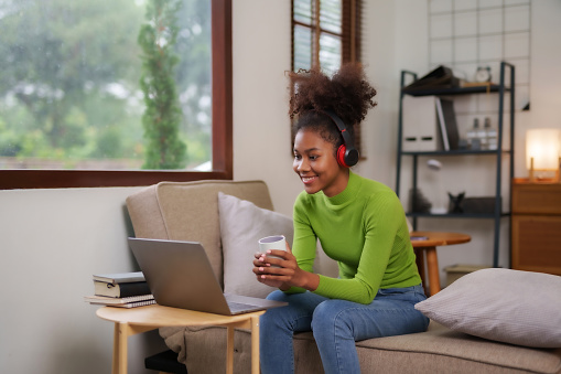 Wanita Muda Afrikaamerika Mengenakan Headphone Menggunakan Laptop Duduk Di Sofa Di Ruang Tamu