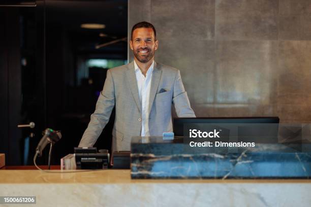 Happy Hotel Receptionist Standing Behind Counter Stock Photo - Download