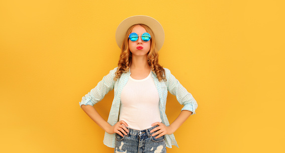 Portrait Of Funny Young Woman Puffs Out Her Cheeks With Curly Hair And Straw Hat On Yellow