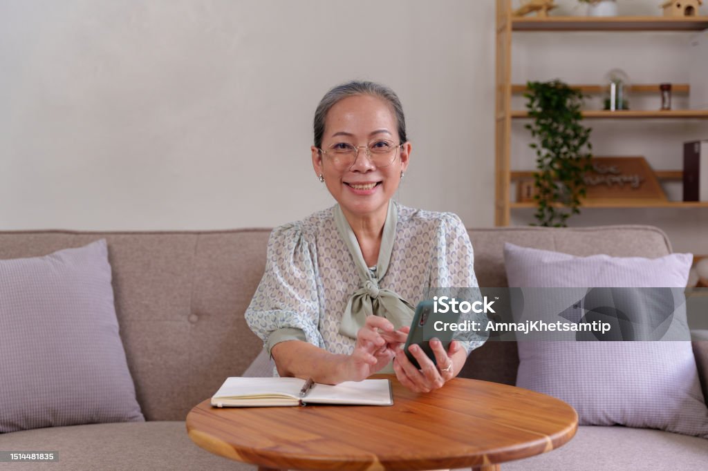 Asian Senile Woman Relaxing At Home Using Mobile Phone In Living Room Playing Social Media On