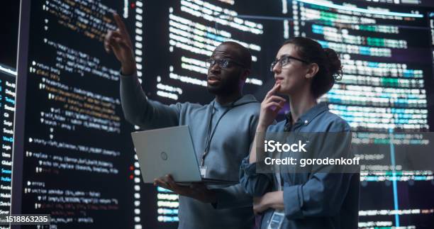 Portrait Of Two Diverse Developers Using Laptop Computer Discussing Lines Of Code That Appear On