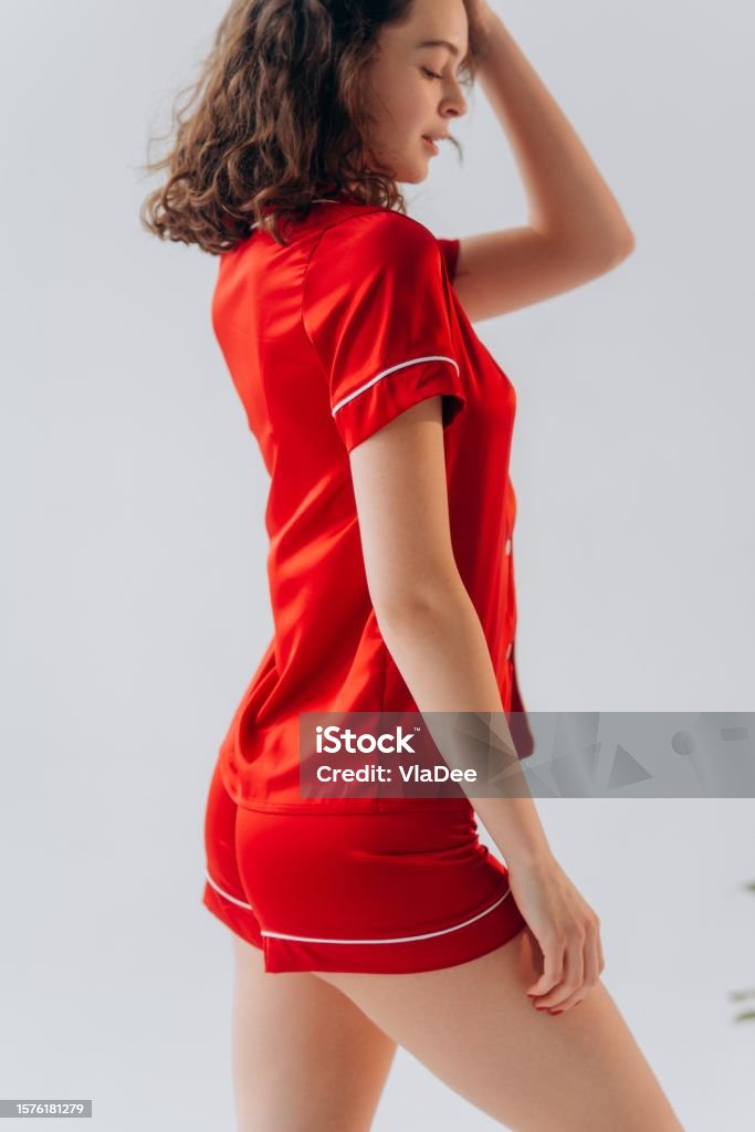 Cheerful Young Woman In Red Pajamas Standing Indoors Against White