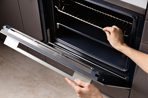 A Girl Opens The Door Of A Builtin Oven With A Display In A Modern