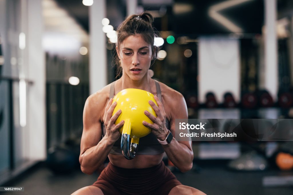 A Focused Beautiful Sportswoman Holding A Yellow Kettlebell While Doing