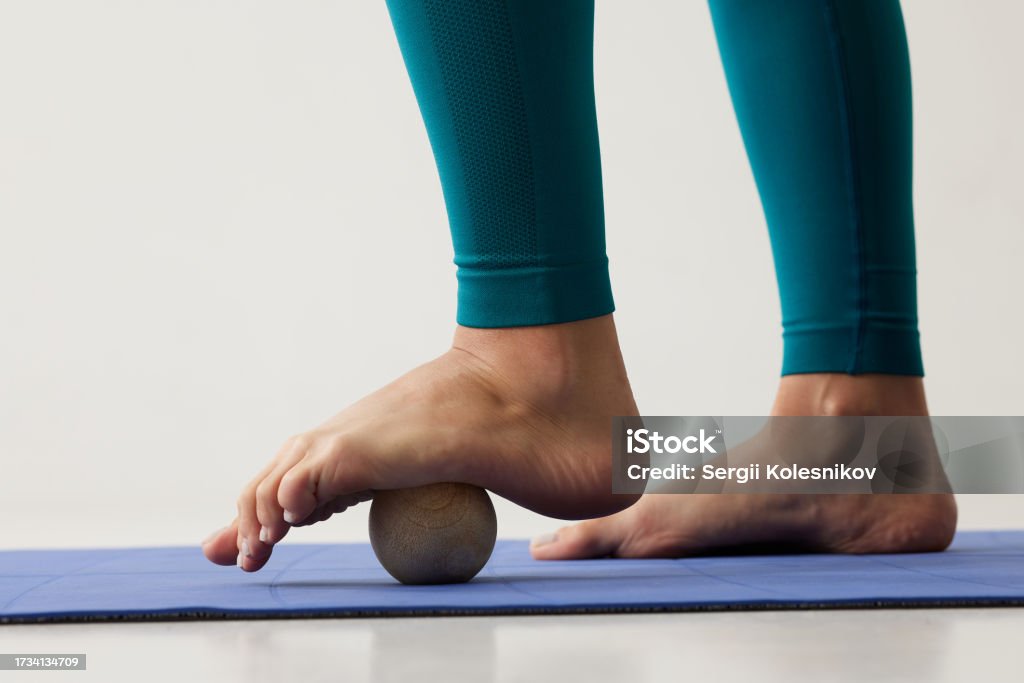 Girl Massaging Her Feet On A Hard Ball Closeup On A White Background