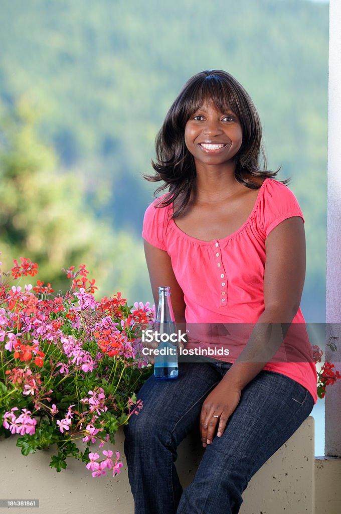 African American Woman Sitting On Balcony Enjoying Mineral Water Stock