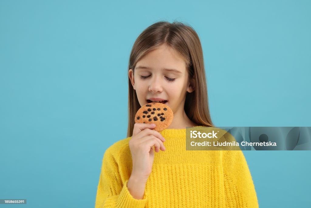 Cute Girl Eating Chocolate Chip Cookie On Light Blue Background Stock