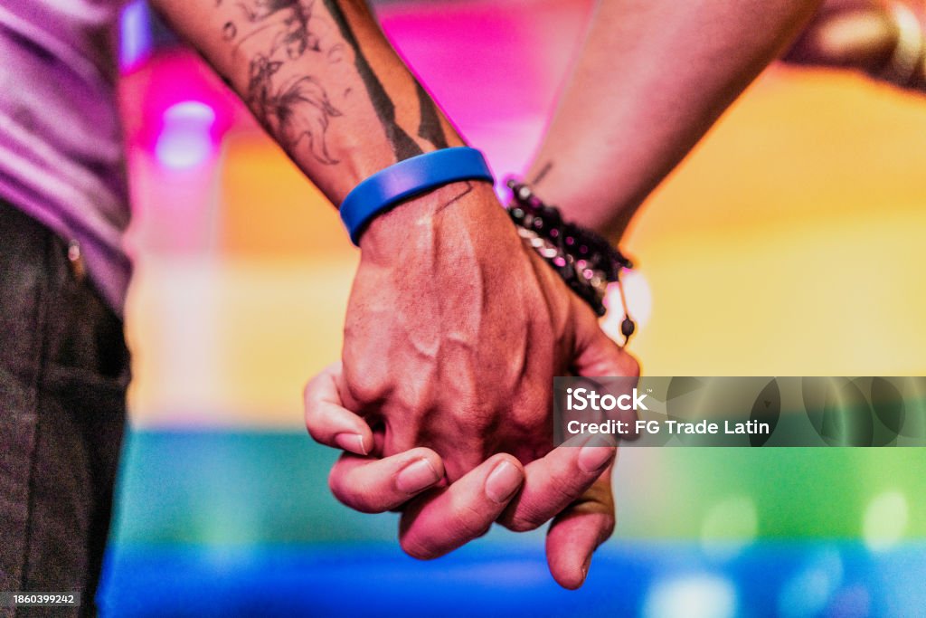 Closeup Of A Gay Couple Holding Hands With Rainbow Flag On Background