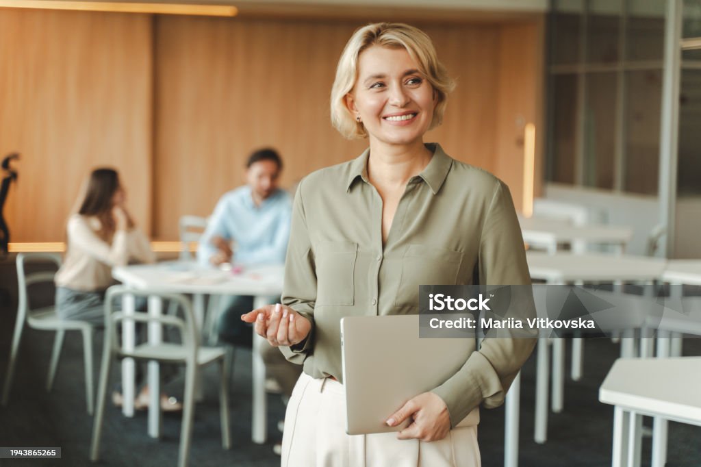 Smiling Middle Aged Businesswoman Holding Laptop Working In Modern