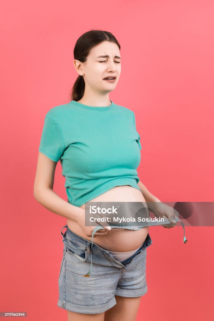 Cropped Image Of Expecting Mother In Unzipped Jeans Measuring Her Pregnant Belly With A Tape