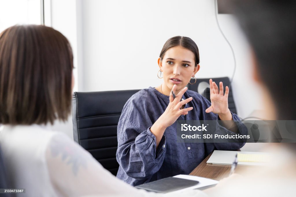 Young Woman Gestures While Explaining New Concept To Female Coworker