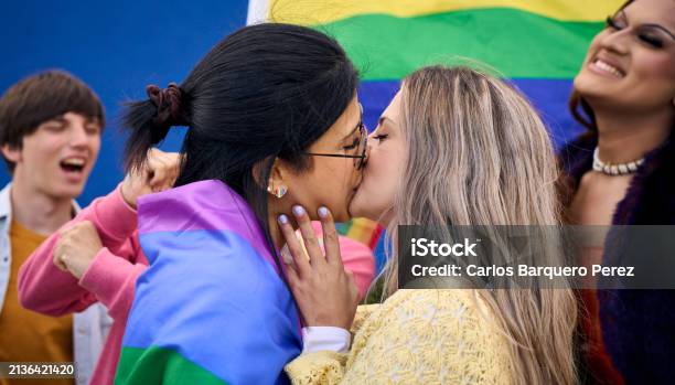 Young Caucasian Lesbian Couple Kissing Lovingly With Rainbow Flags