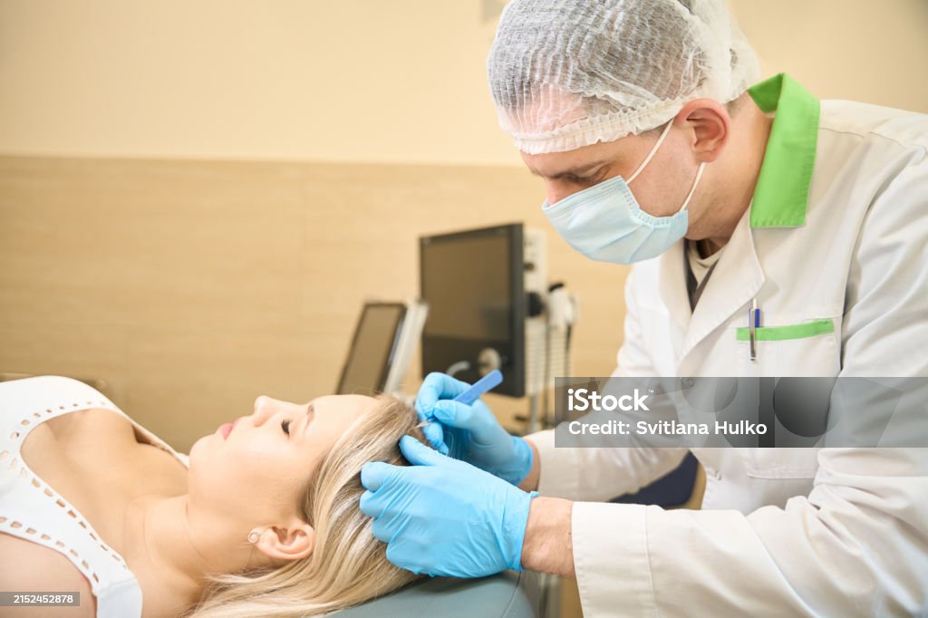 Dermatologic Surgeon Removing Atheroma On Female Patient Scalp Using