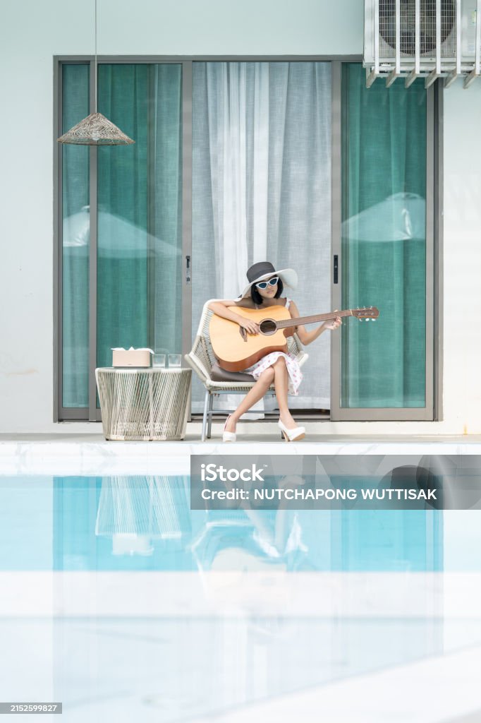 Asian Female Tourist Sits Near The Poolside Playing The Guitar And