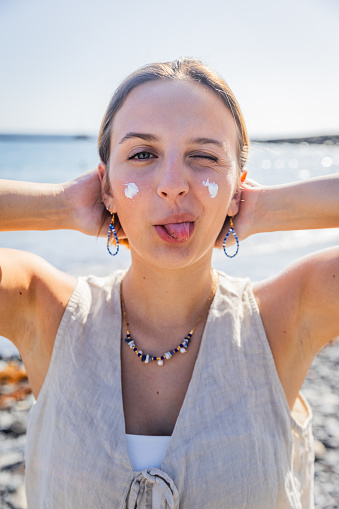 A Woman Is Standing On A Beach Sticks Her Tongue Out While She Has Suncream On Her Face Stock