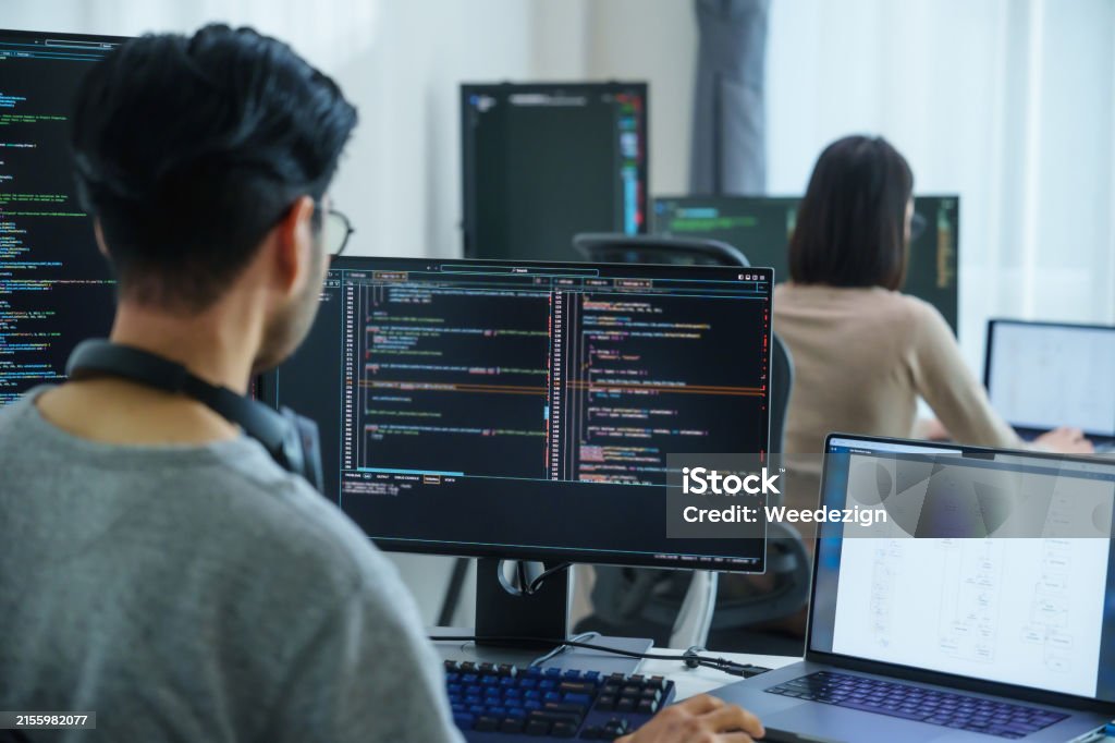 Asian Software Developers Working On Multiple Screens Displaying Code And Application Diagrams