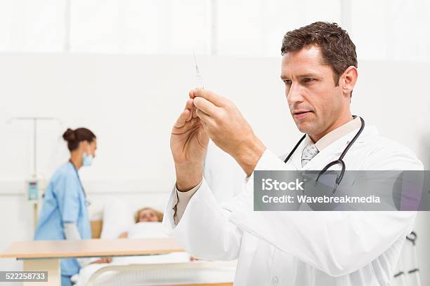 Dokter Memegang Suntikan Dengan Kolega Dan Pasien Di Belakang Foto Stok ... Dokter Memegang Suntikan Dengan Kolega Dan Pasien Di Belakang Foto Stok ...