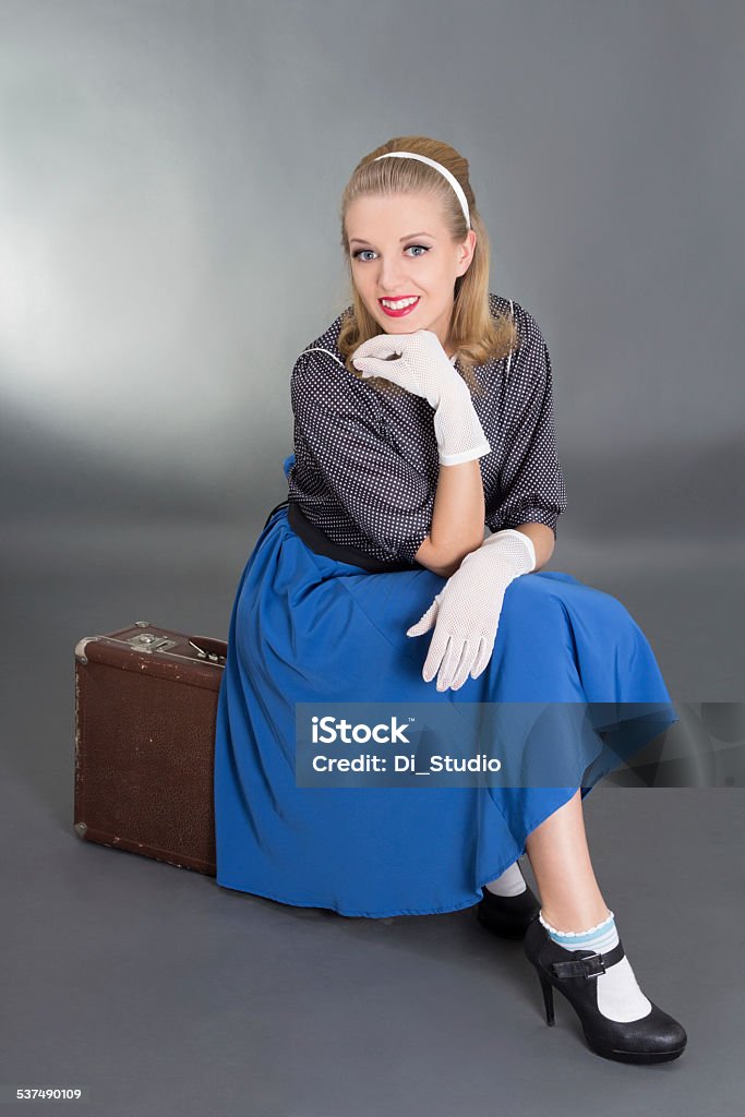 Young Beautiful Pinup Girl Sitting On Retro Suitcase Over Grey Stock