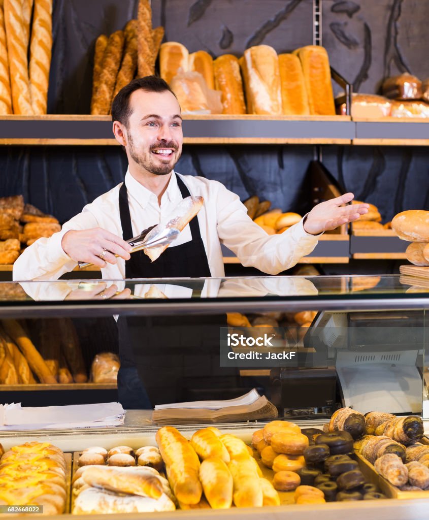 Male Shop Assistant Demonstrating Fresh Delicious Pastry In Bakery