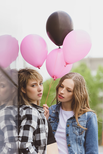 Lesbian Couple Standing Together And Holding Air Balloons Outdoors