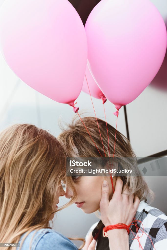 Young Lesbian Couple Kissing And Holding Air Balloons Outdoors Stock