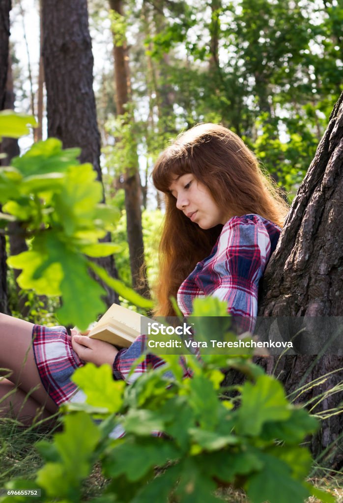 Gadis Berambut Merah Yang Cantik Duduk Di Bawah Pohon Dan Membaca Buku ... Gadis Berambut Merah Yang Cantik Duduk Di Bawah Pohon Dan Membaca Buku ...