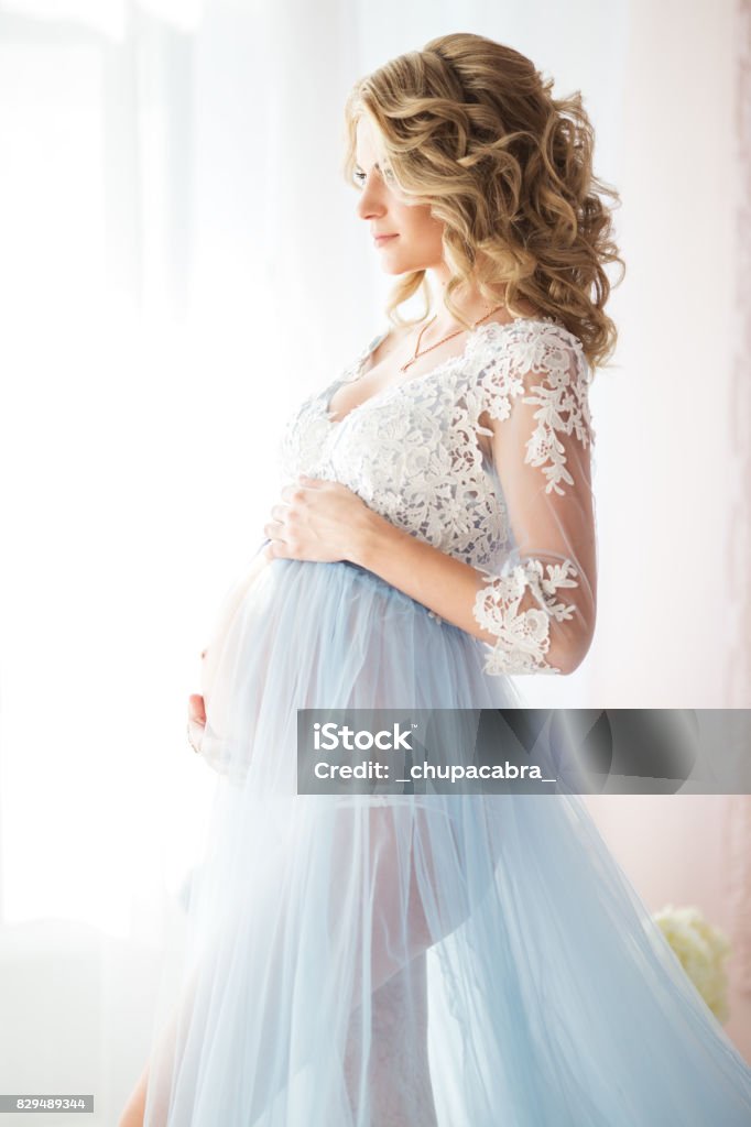 Pretty Smiling Pregnant Girl Is Wearing Blue Boudoir Dress Sitting In