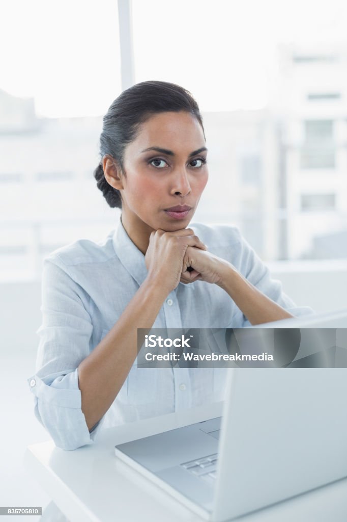 Serious Dark Haired Woman Looking At Camera Sitting At Her Desk Stock