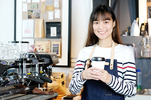 젊은 아시아 여성 들고 걸릴 멀리 커피 바리 스타 카페 카운터 배경 중소 기업 소유자 음식 및 음료 산업 개념에 얼굴을 웃는 컵