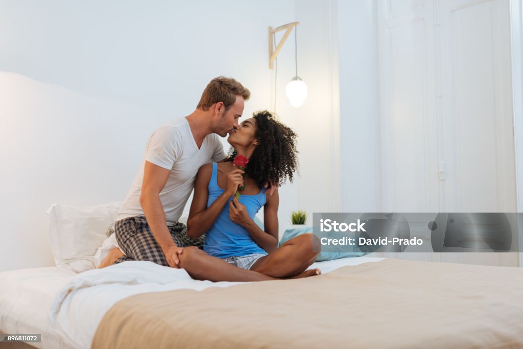 Young Beautiful Interracial Couple In Bed Giving A Surprise Rose Stock