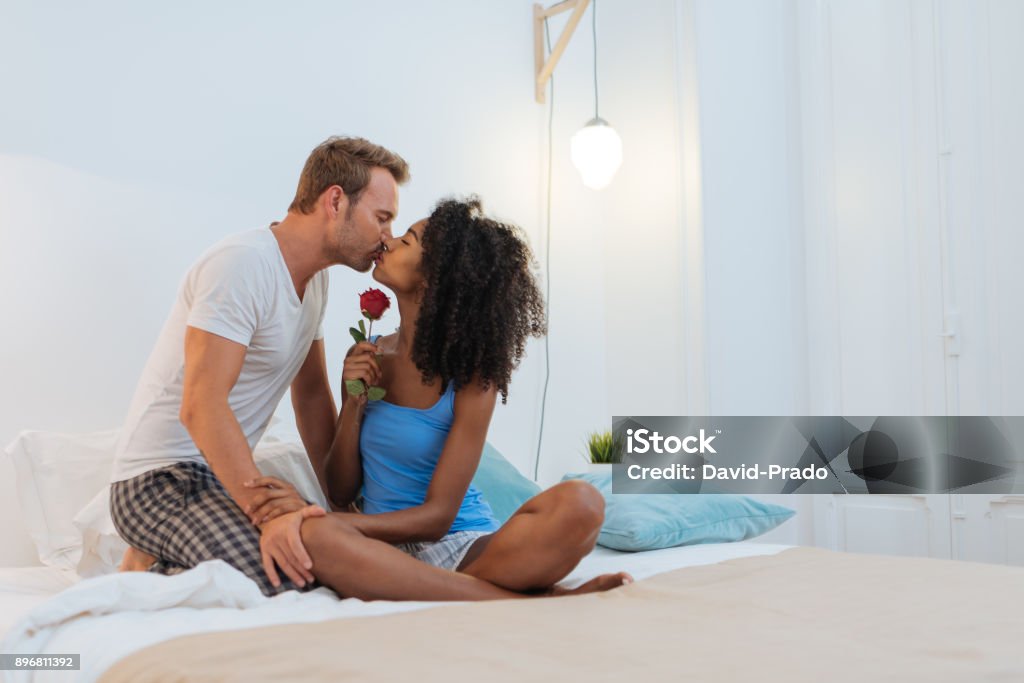Young Beautiful Interracial Couple In Bed Giving A Surprise Rose Stock