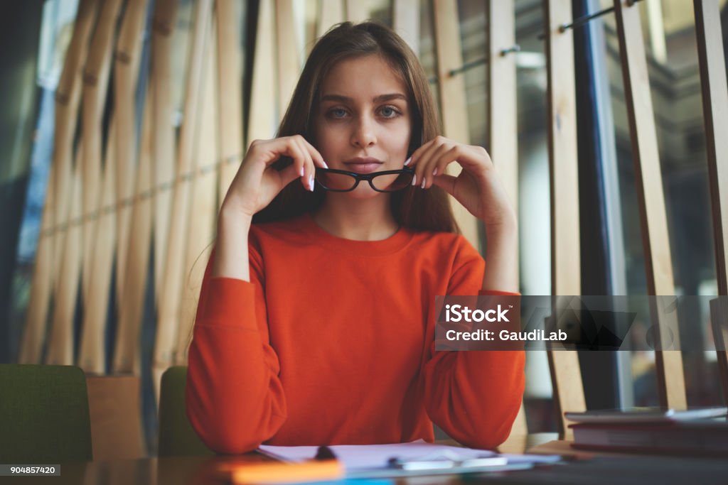 매력적인 지능형 Hipster 소녀 손에 더 나은 비전을 위한 세련 된 광학 안경을 잡고 카메라를 보고 트렌디한 블랙 프레임