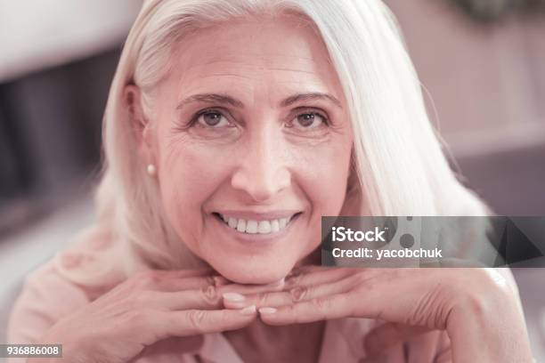 Satisfied Kind Woman Holding Hands Together Under Chin And Smiling