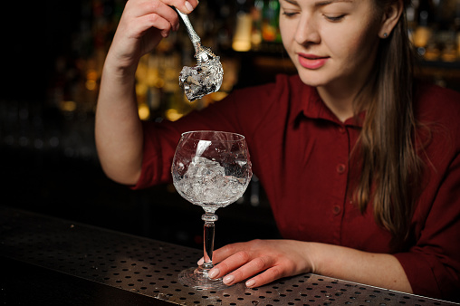 Beautiful Female Barman Putting Ice Cubes Into A Glass Making An Aperol